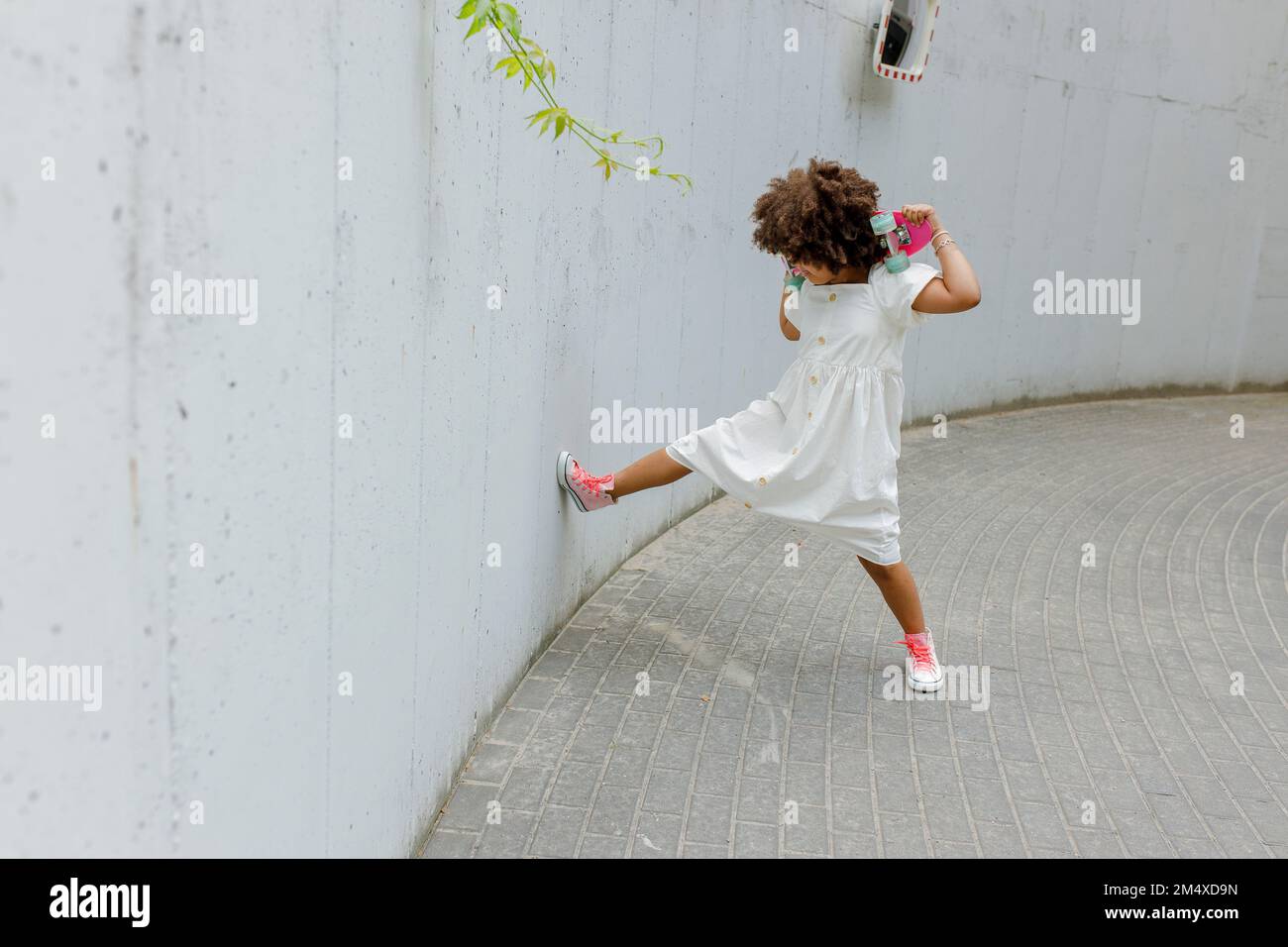 Girl standing with skateboard and kicking wall at footpath Stock Photo ...