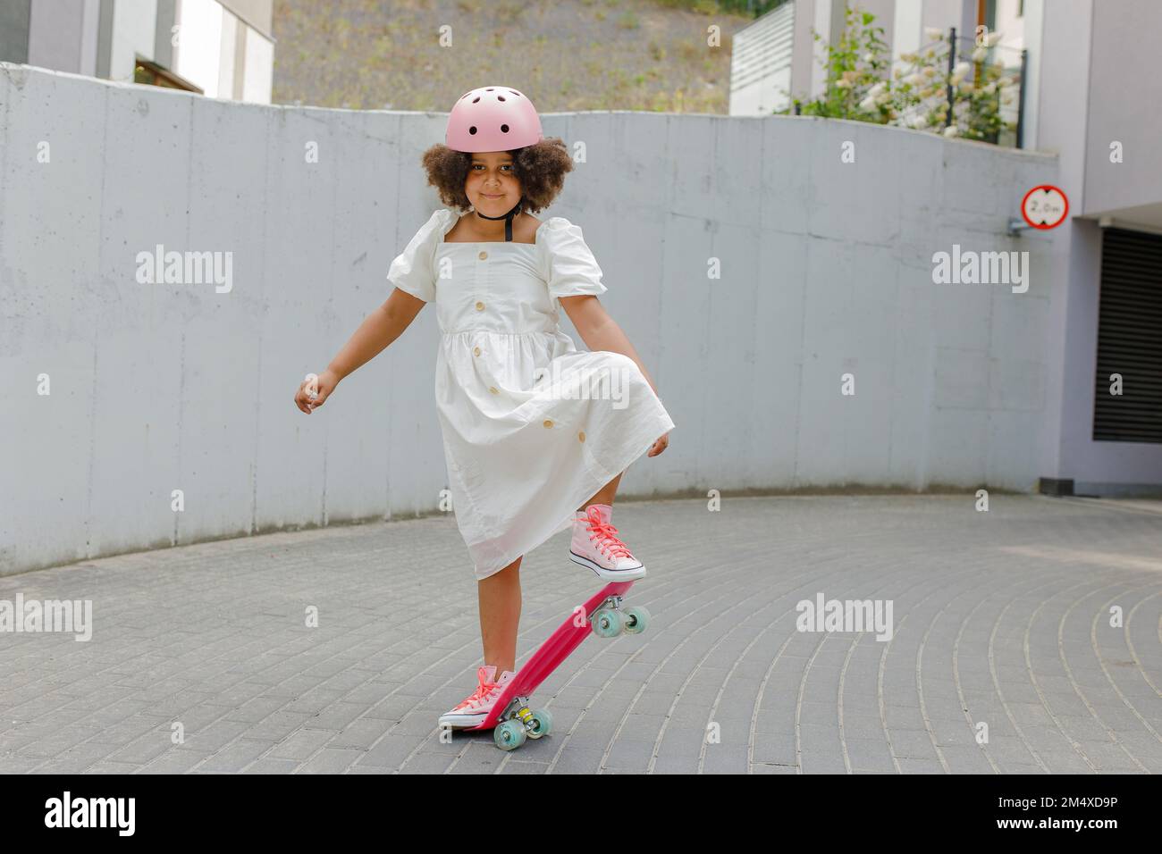 Smiling girl wearing helmet skateboarding on footpath Stock Photo - Alamy