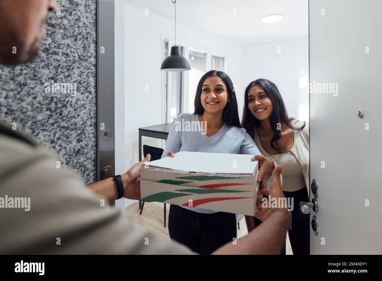 Smiling young women receiving pizza from delivery person Stock Photo ...