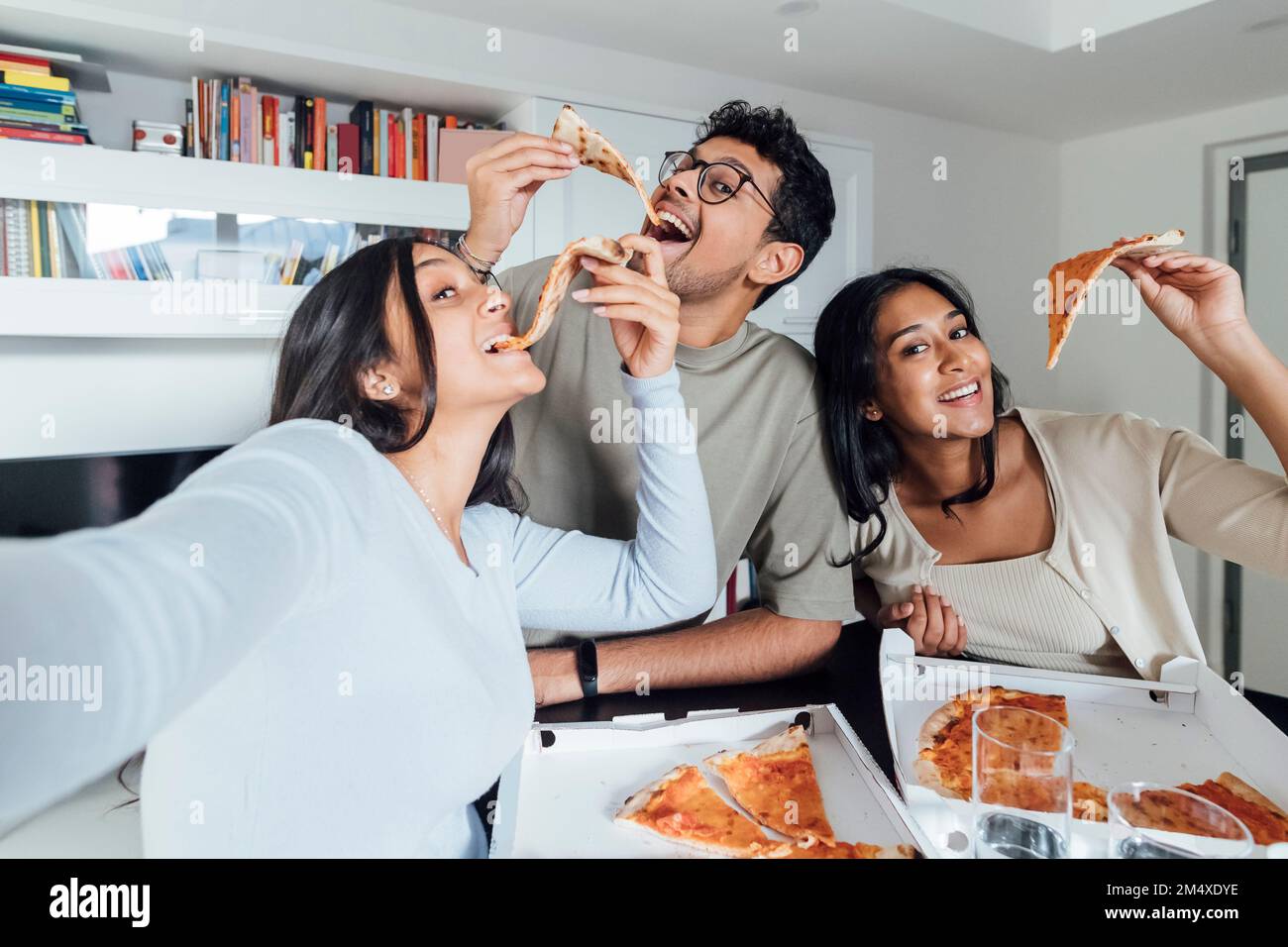 Happy young woman taking selfie with woman and man having pizza at home ...
