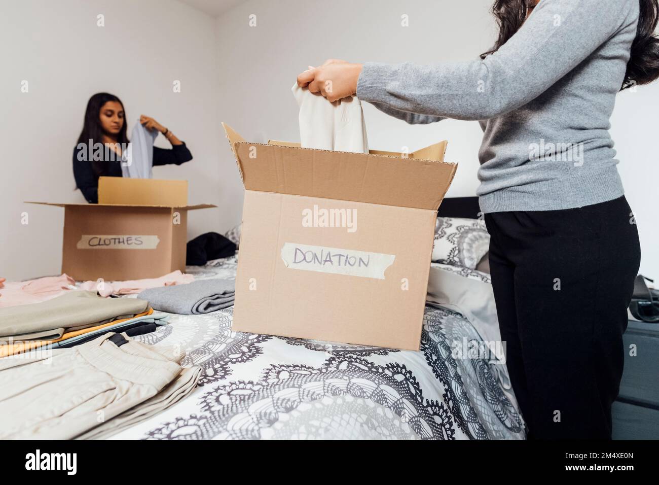 Young women packing box of clothes for donation on bed at home Stock ...