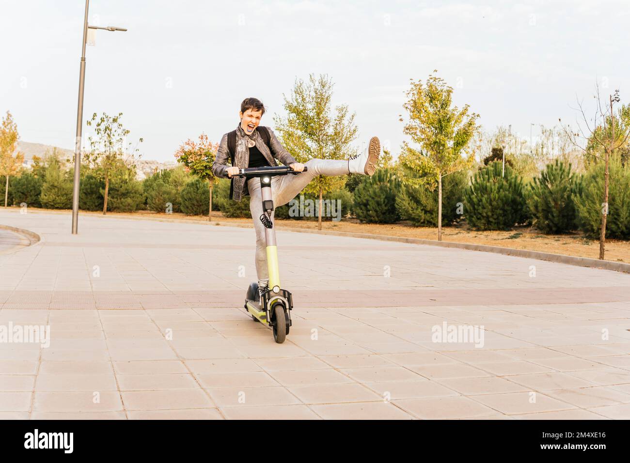 Playful woman riding electric push scooter with leg up Stock Photo - Alamy