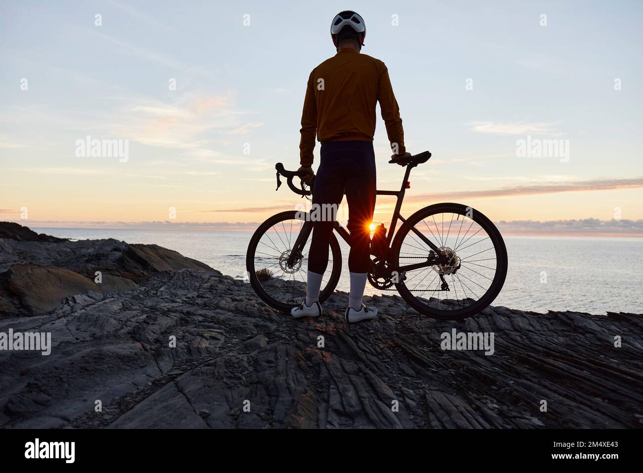 Cyclist standing with bicycle in front of sea at sunrise Stock Photo ...