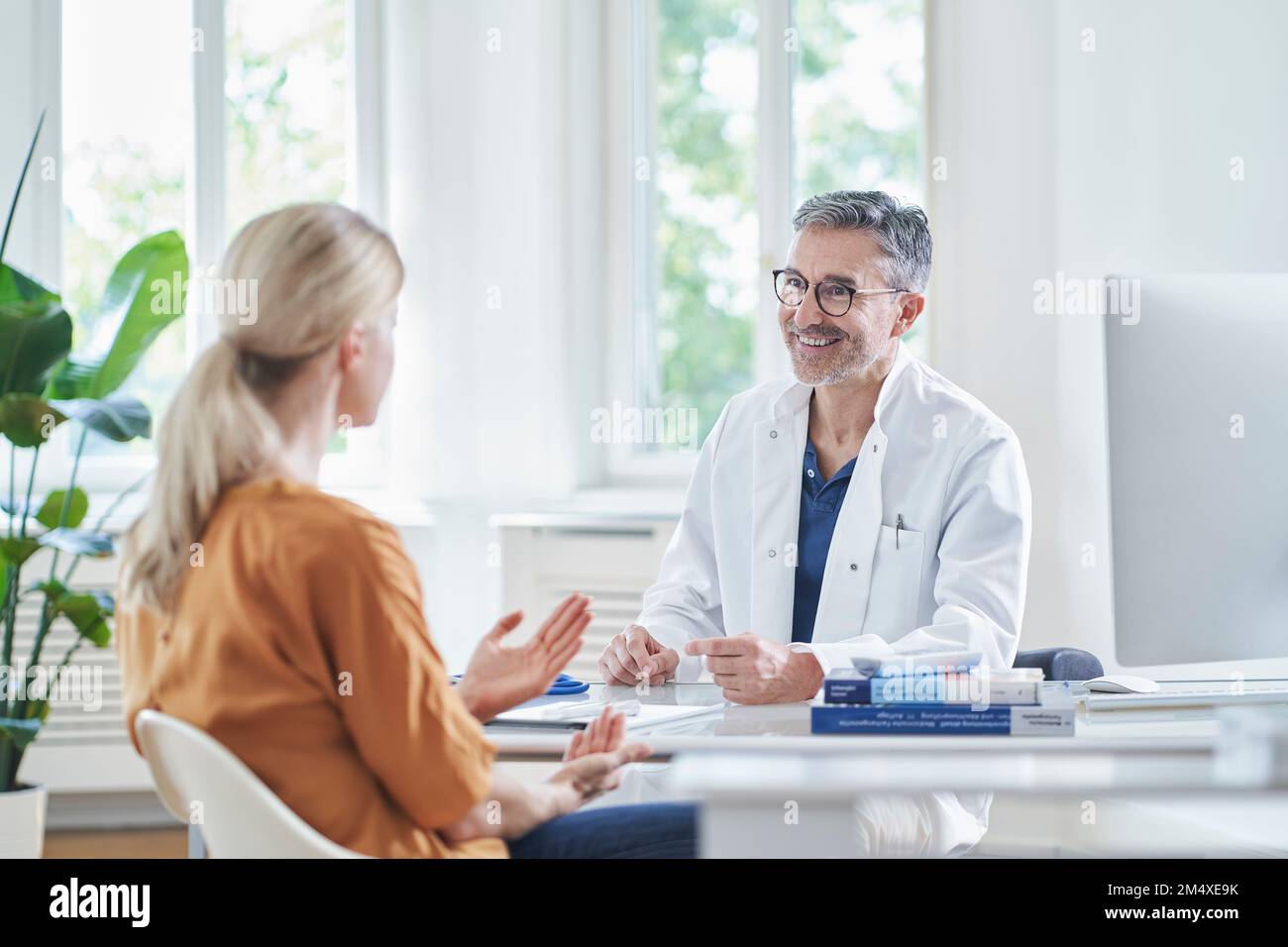 Happy doctor with patient sitting at desk in medical practice Stock ...