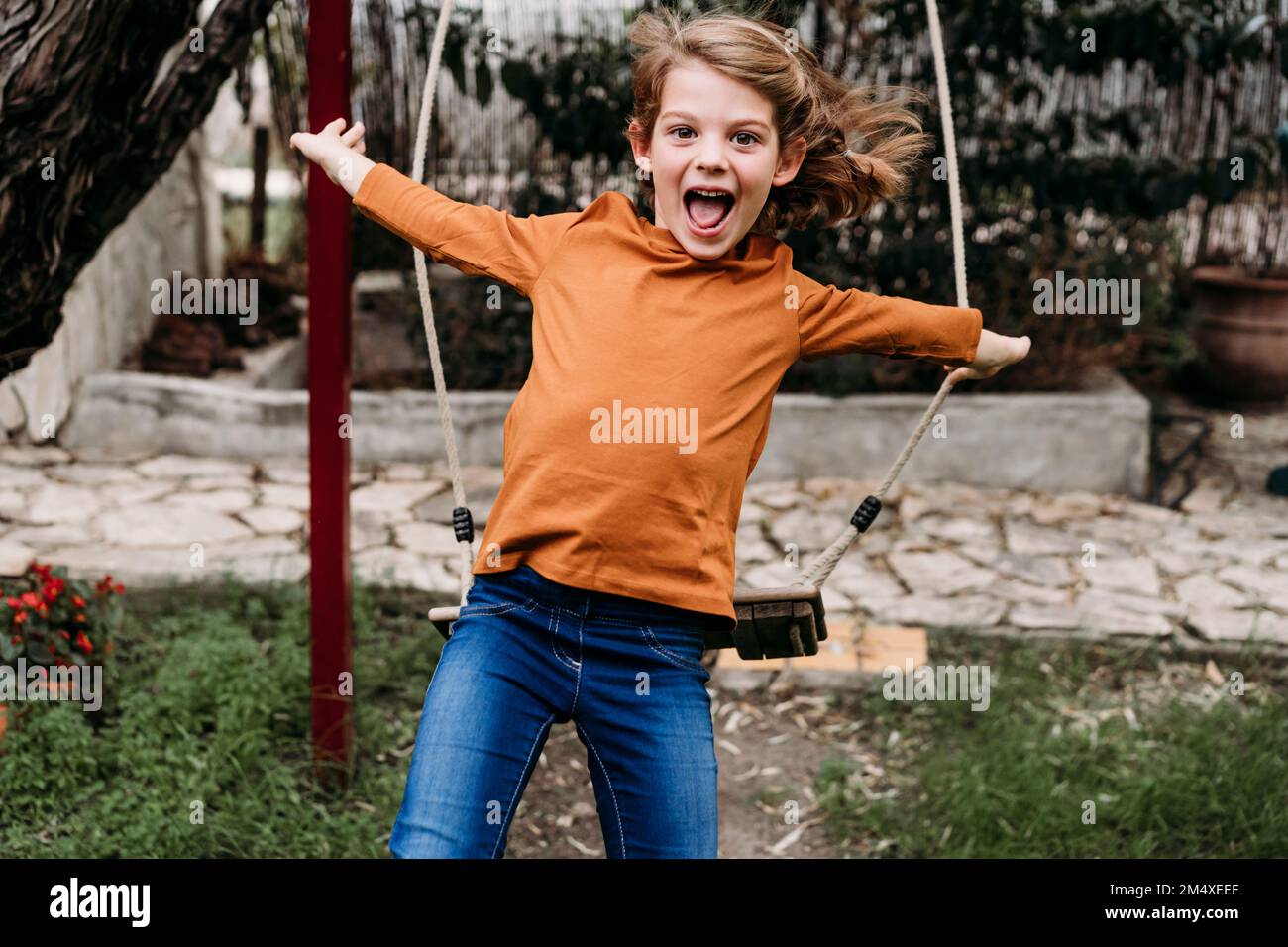 Playful girl jumping from swing in garden Stock Photo - Alamy