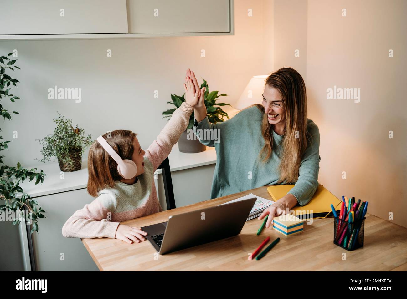Happy mother giving high-five to daughter sitting with laptop at table ...