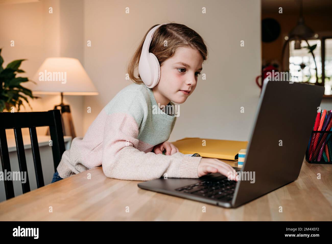 Girl wearing wireless headphones using laptop on table at home Stock ...