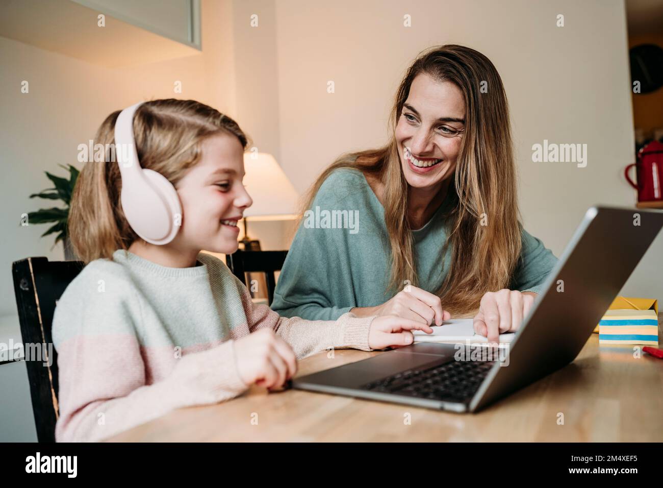 Happy mother helping daughter studying through laptop on table Stock ...