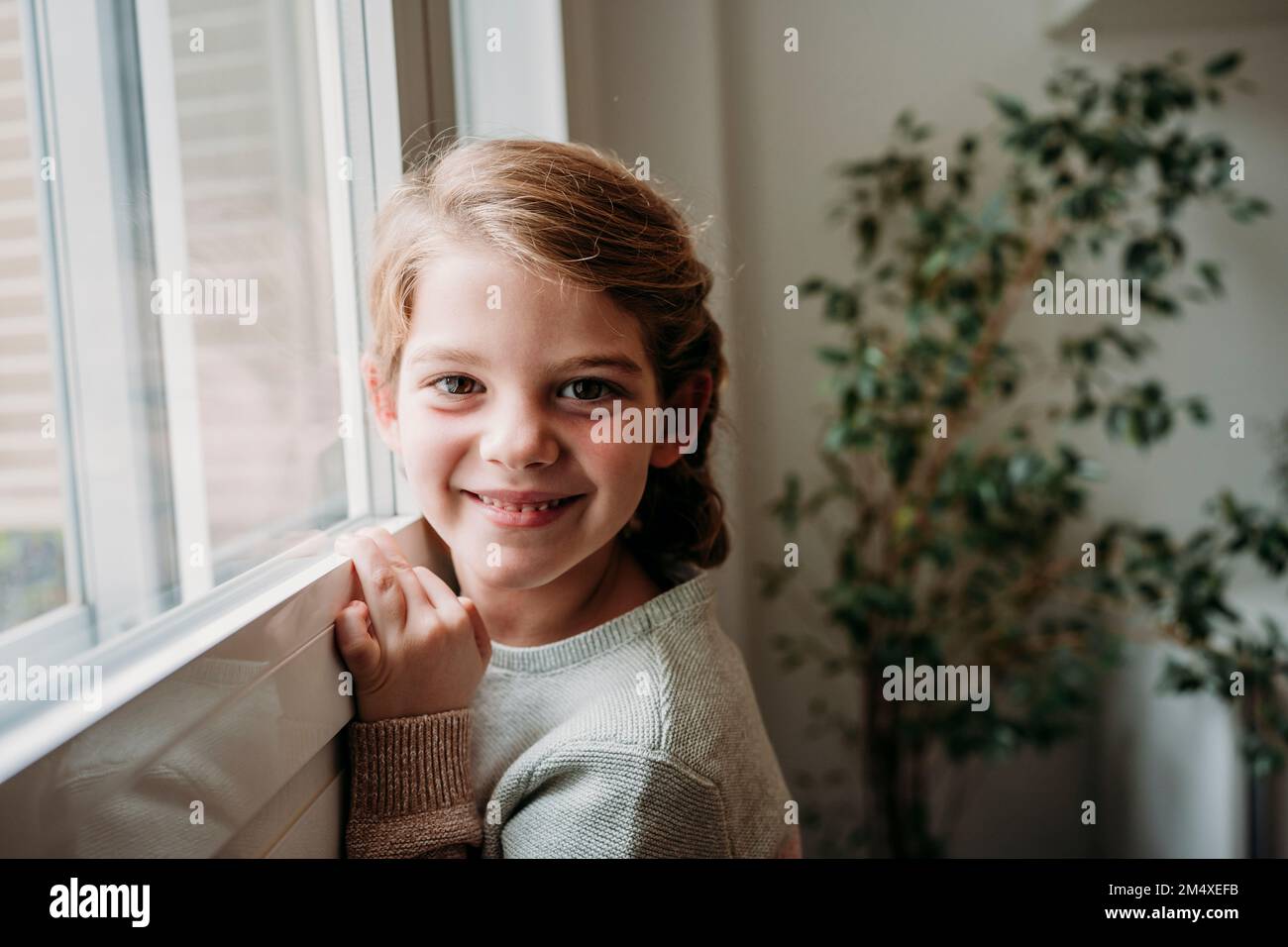 Happy cute girl by window at home Stock Photo - Alamy