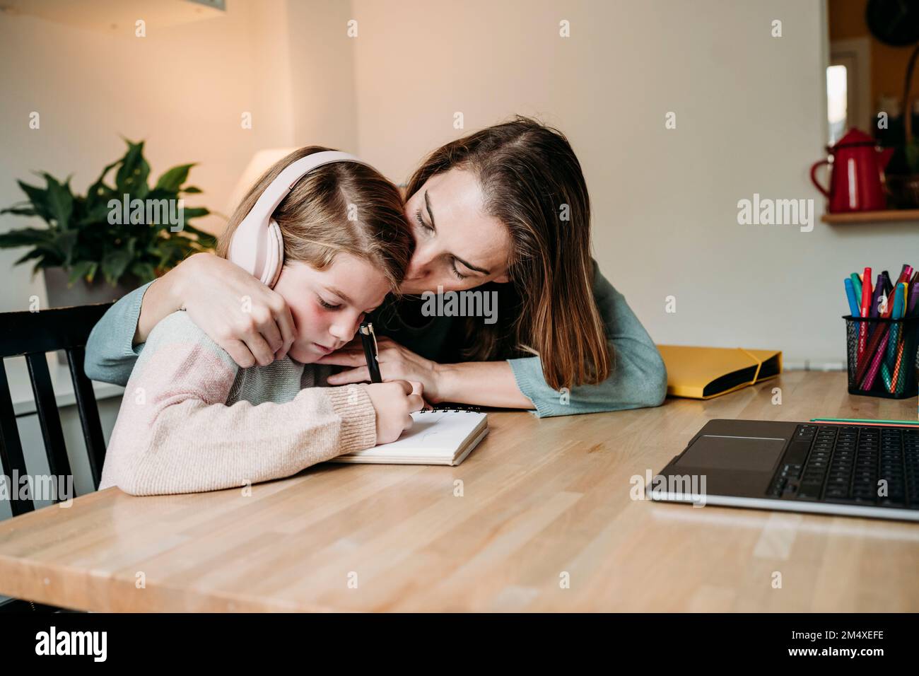 Mother kissing daughter doing homework at table at home Stock Photo - Alamy