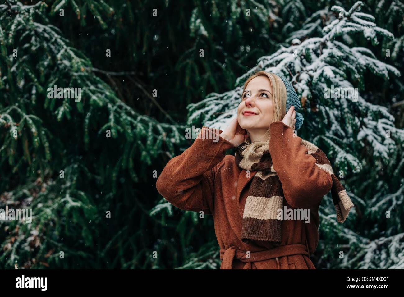 Smiling woman wearing warm clothing in front of fir tree Stock Photo ...