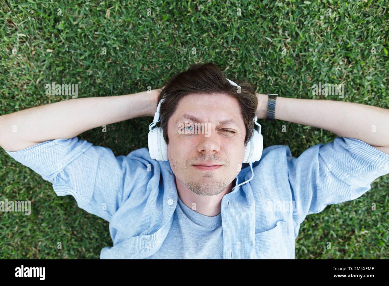 Smiling man listening to music through headphones and relaxing in grass ...