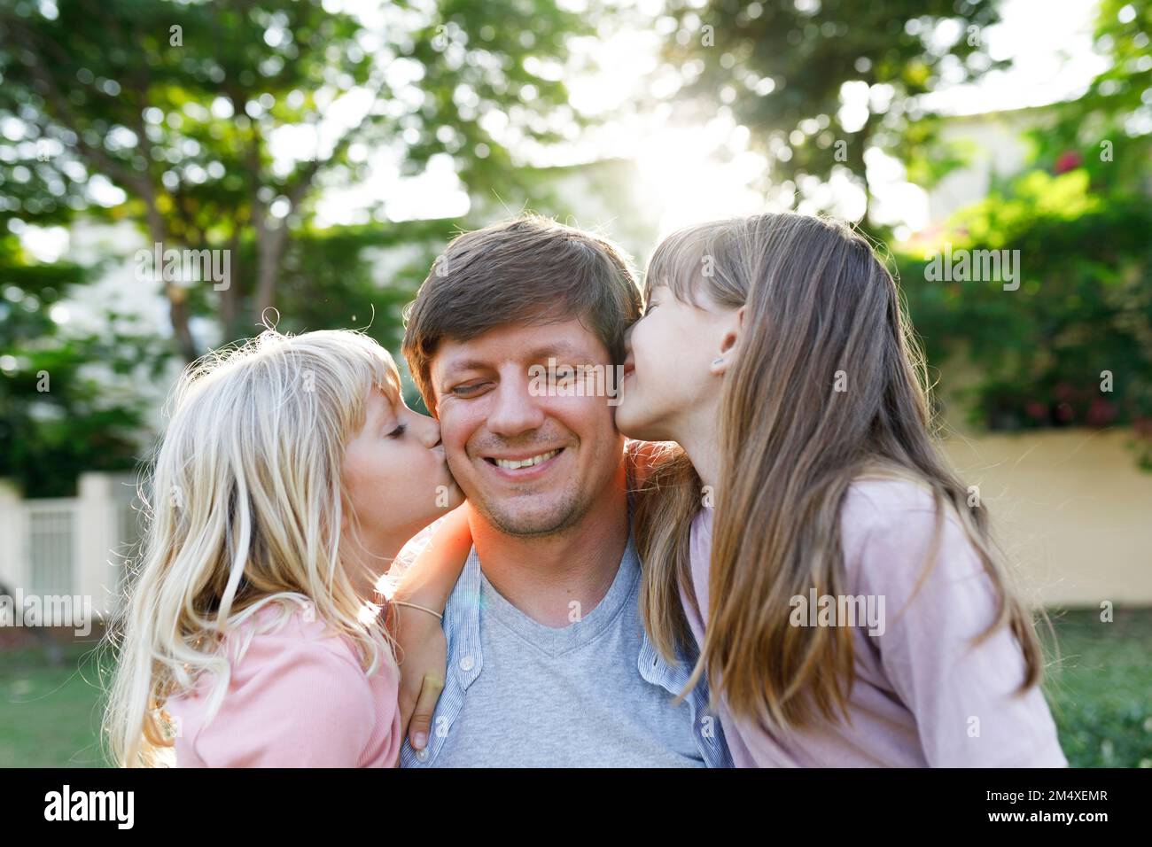 Smiling father with daughters kissing him on cheek at park Stock Photo ...