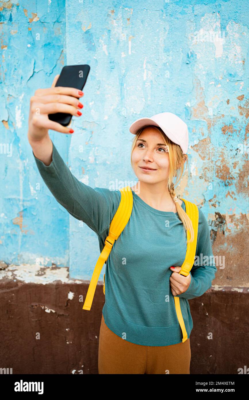Smiling woman with backpack taking selfie through smart phone Stock ...