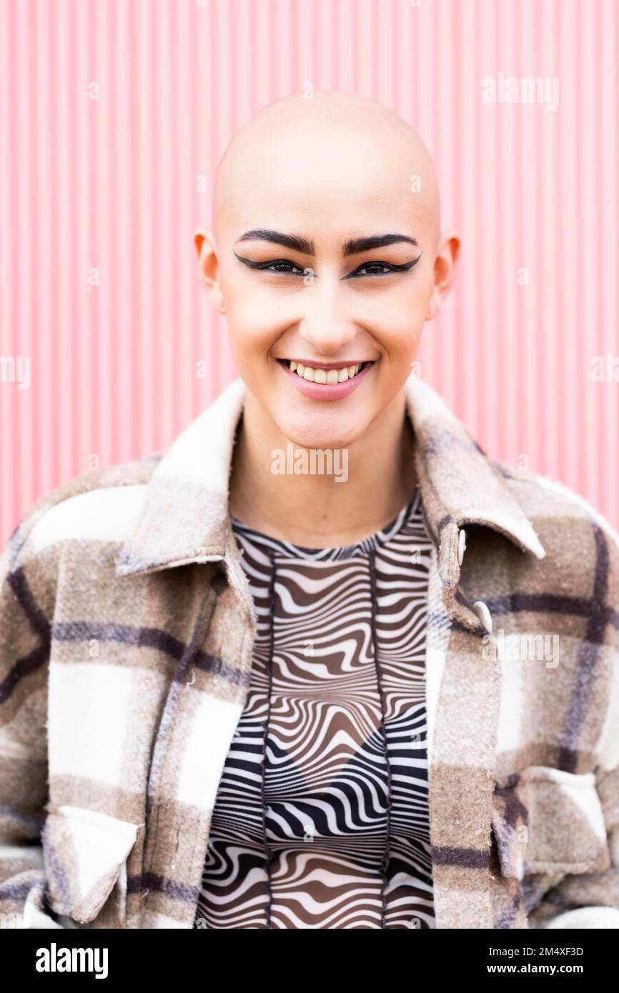Cheerful young woman with shaved head in front of pink wall Stock Photo ...