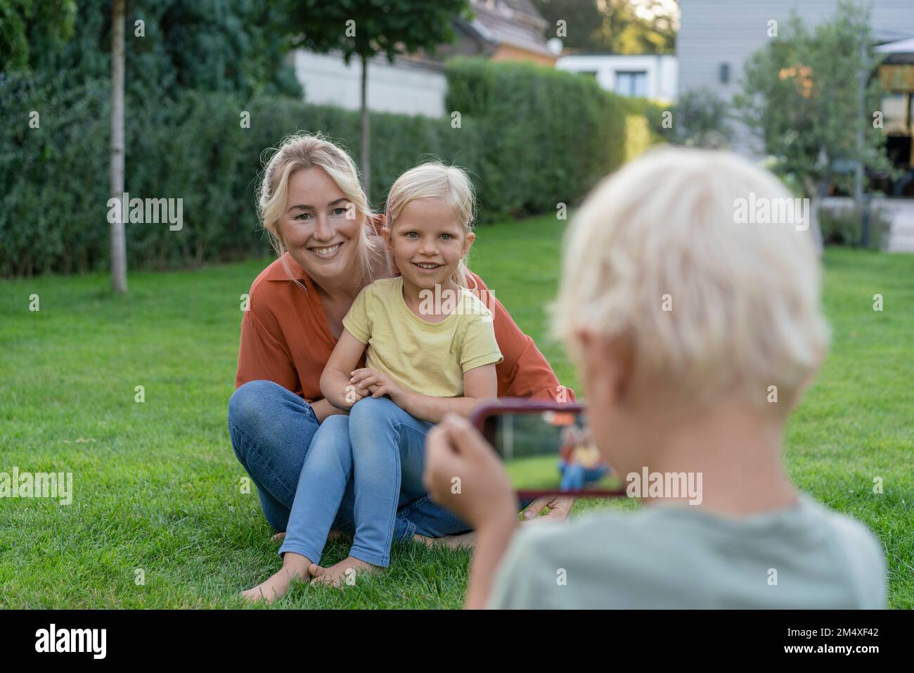 Boy photographing smiling mother and sister through smart phone in ...
