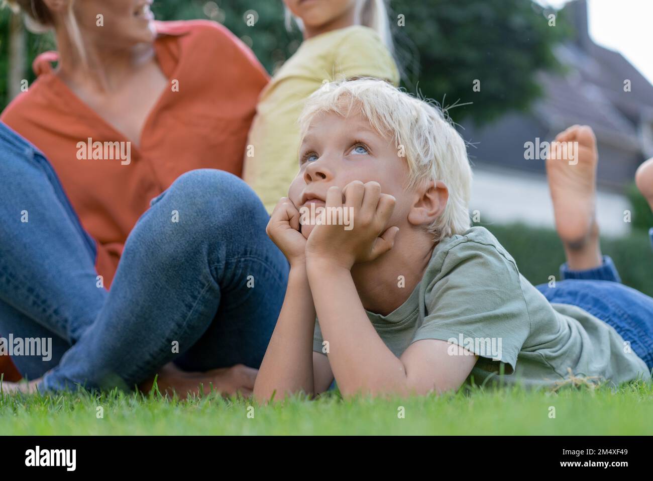 Thoughtful boy leaning on elbow by mother and sister in garden Stock ...