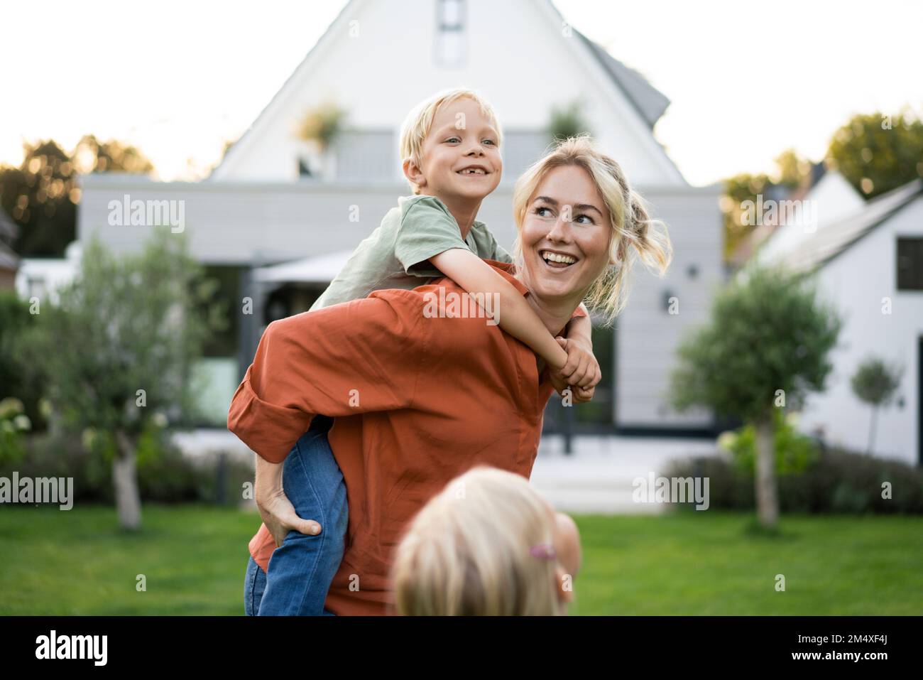 Happy mother giving piggyback ride to daughter in back yard Stock Photo ...