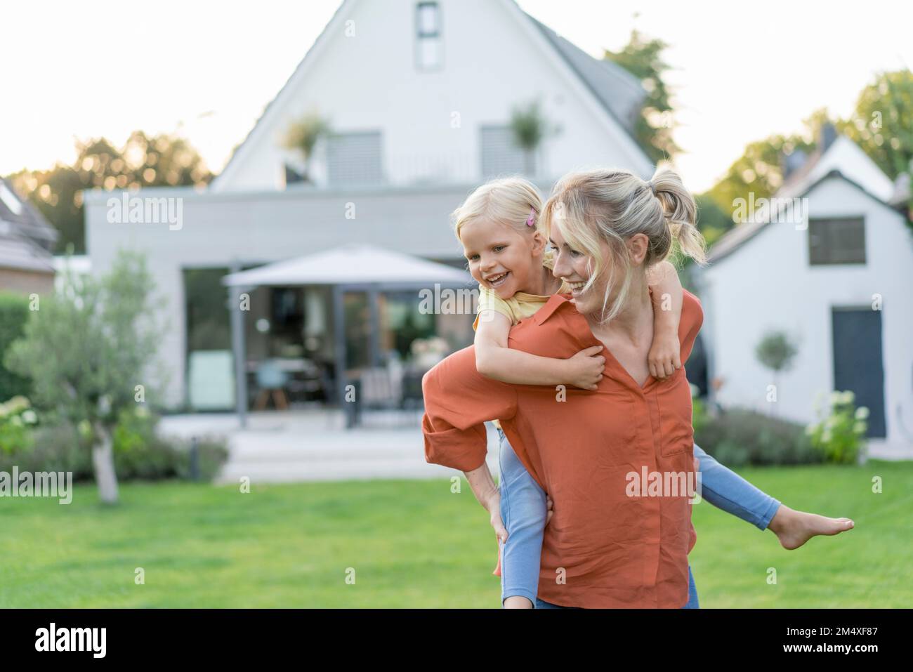 Happy mother giving piggyback ride to daughter in garden Stock Photo ... Happy mother giving piggyback ride to daughter in garden Stock Photo ...