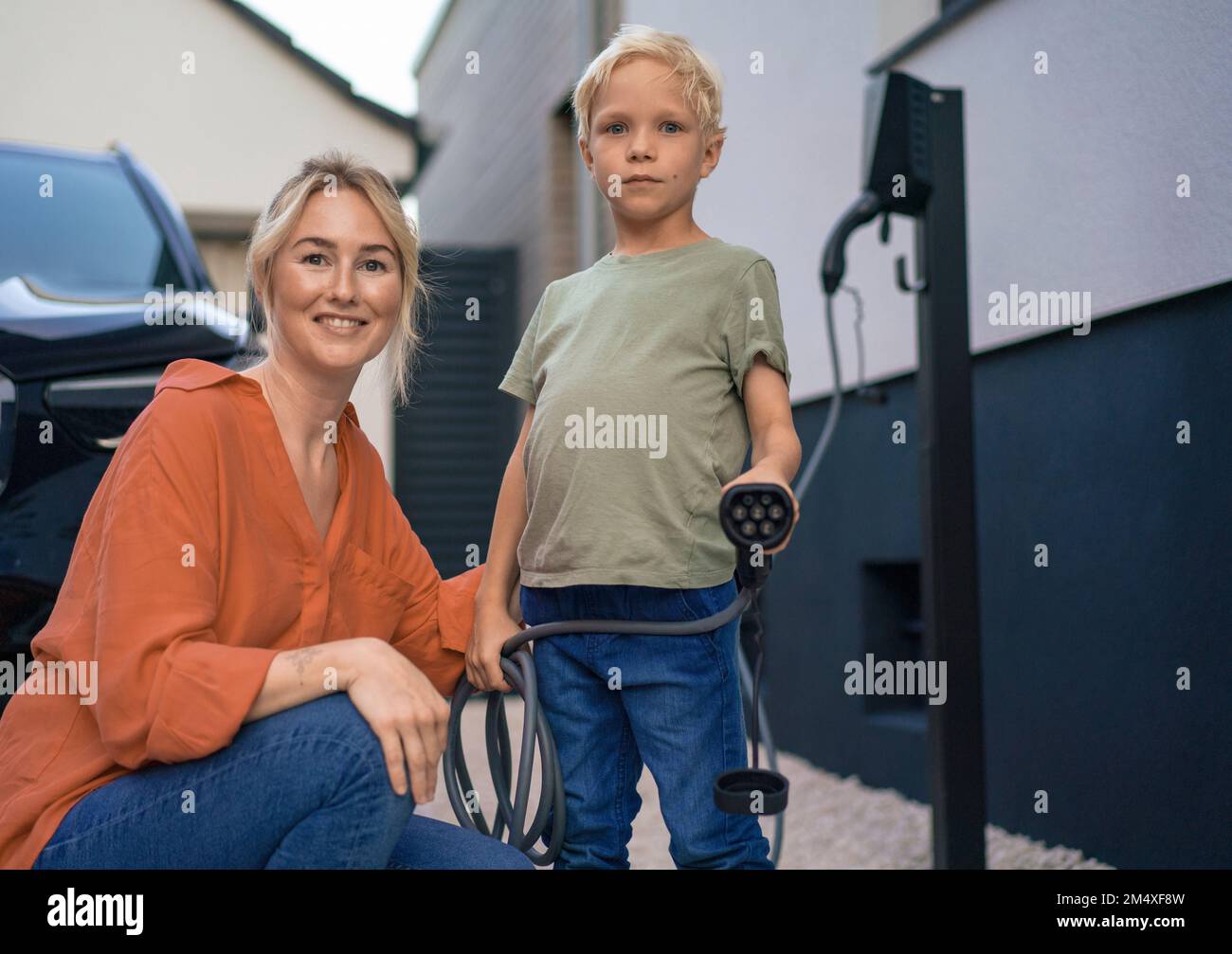 Boy holding electric vehicle charger plug by mother in front yard Stock ...