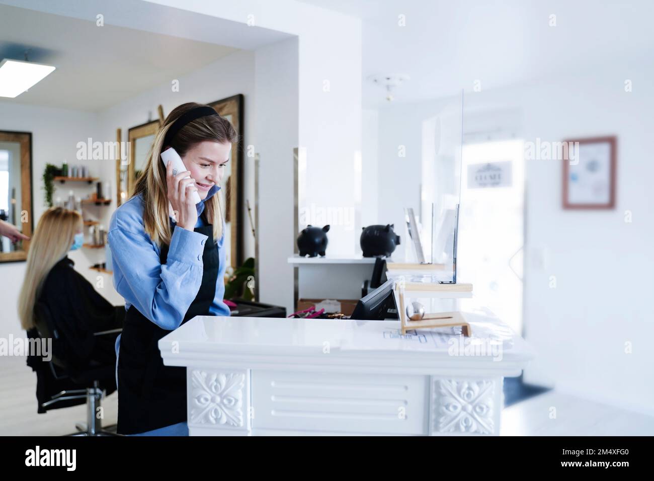 Smiling hairdresser talking on phone at reception desk in salon Stock ...