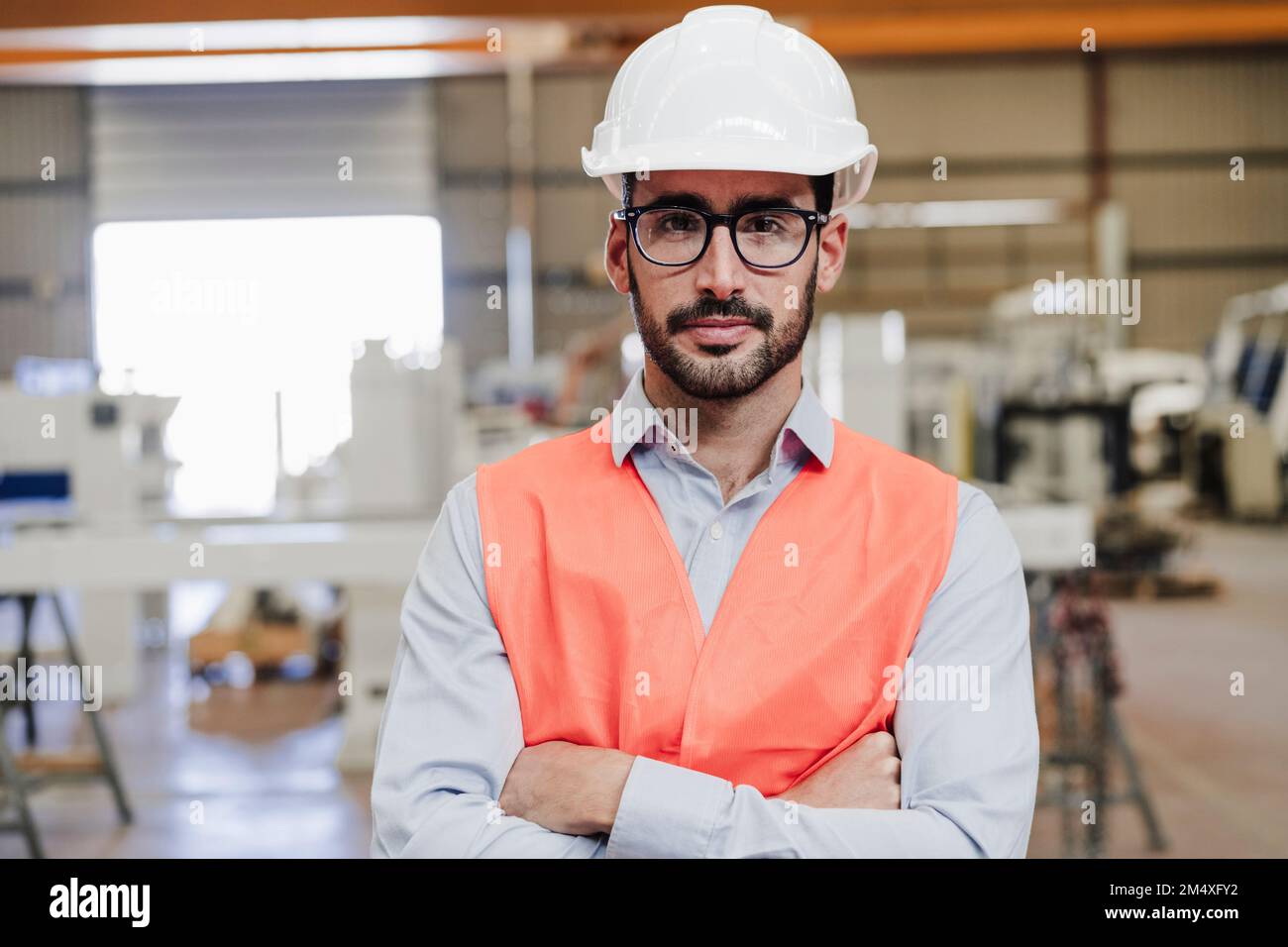 Confident engineer wearing eyeglasses and protective workwear standing ...