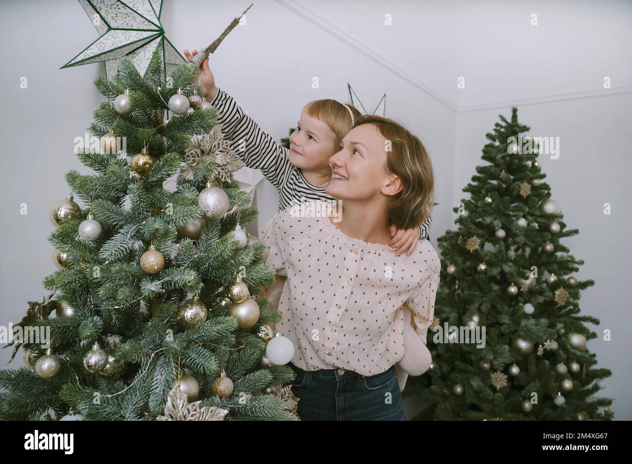 Smiling mother giving daughter piggyback ride to put star on Christmas ...