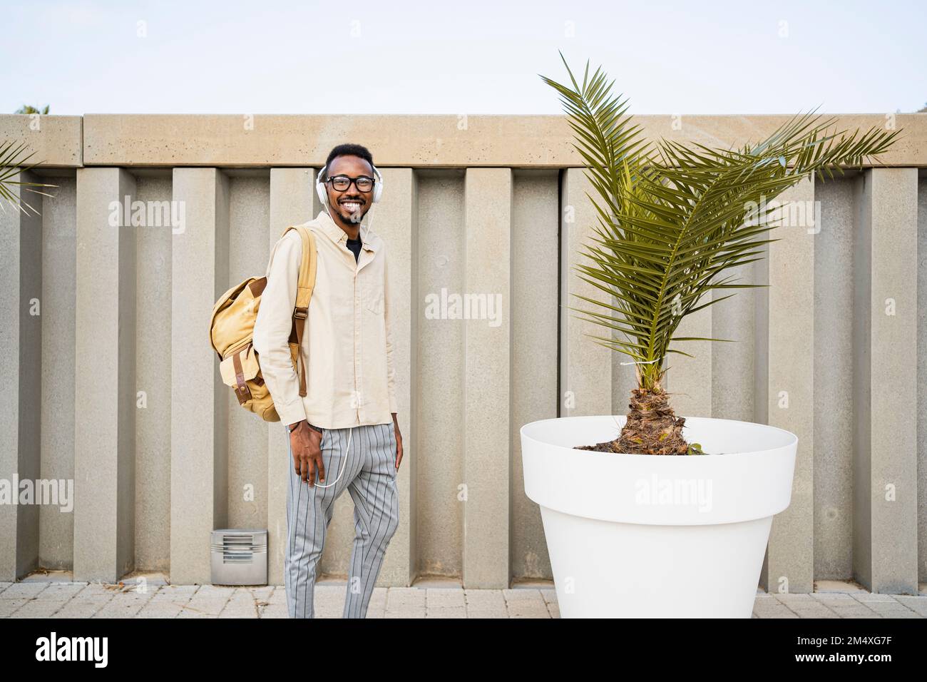 Happy man wearing backpack standing by plant in front of wall Stock ...