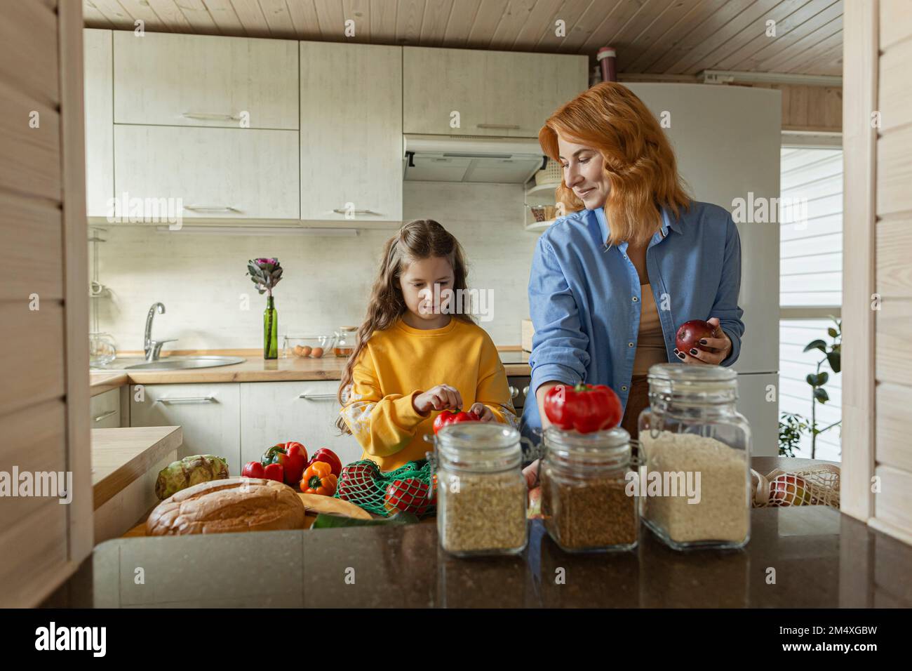 Mother and daughter unpacking fresh groceries in kitchen Stock Photo ...