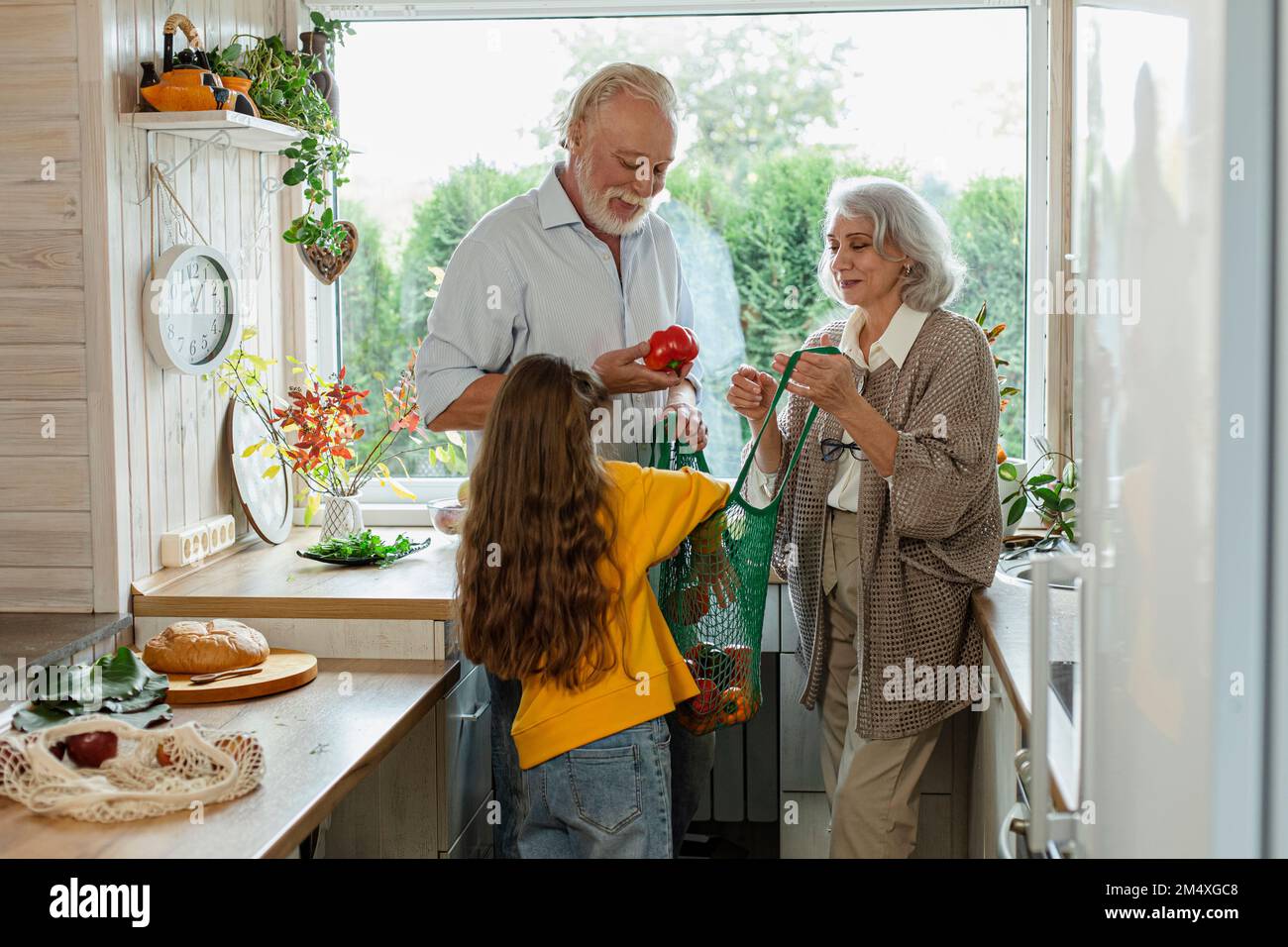 Grandparents and granddaughter unpacking fresh groceries in kitchen ...