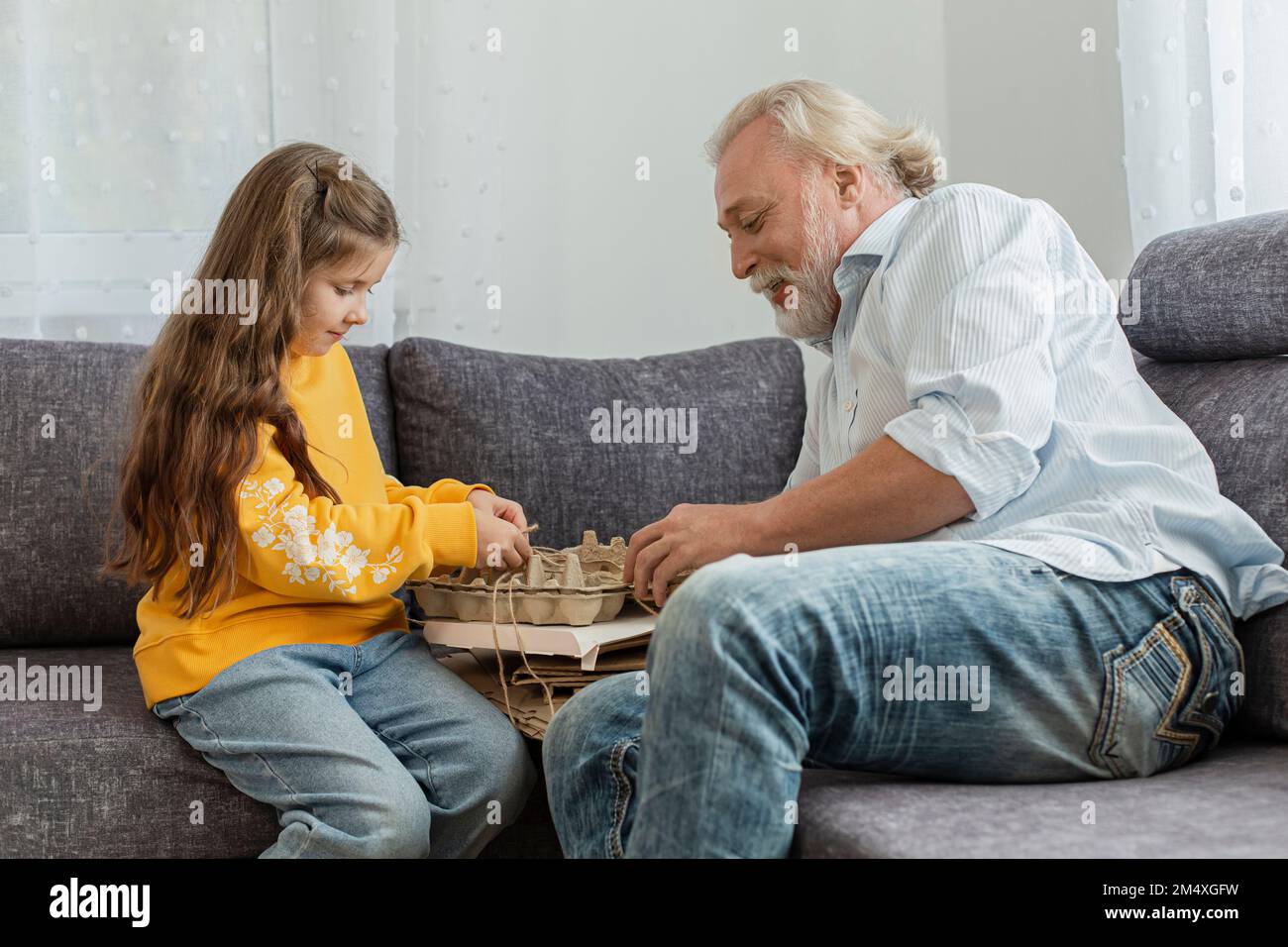 Grandfather and granddaughter bunching waste paper together on sofa ...