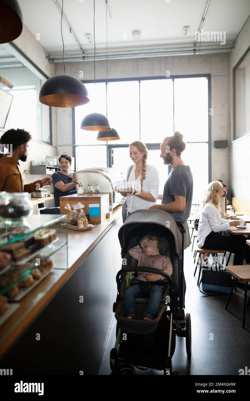 Smiling parents with daughter in stroller ordering at coffee shop Stock ...