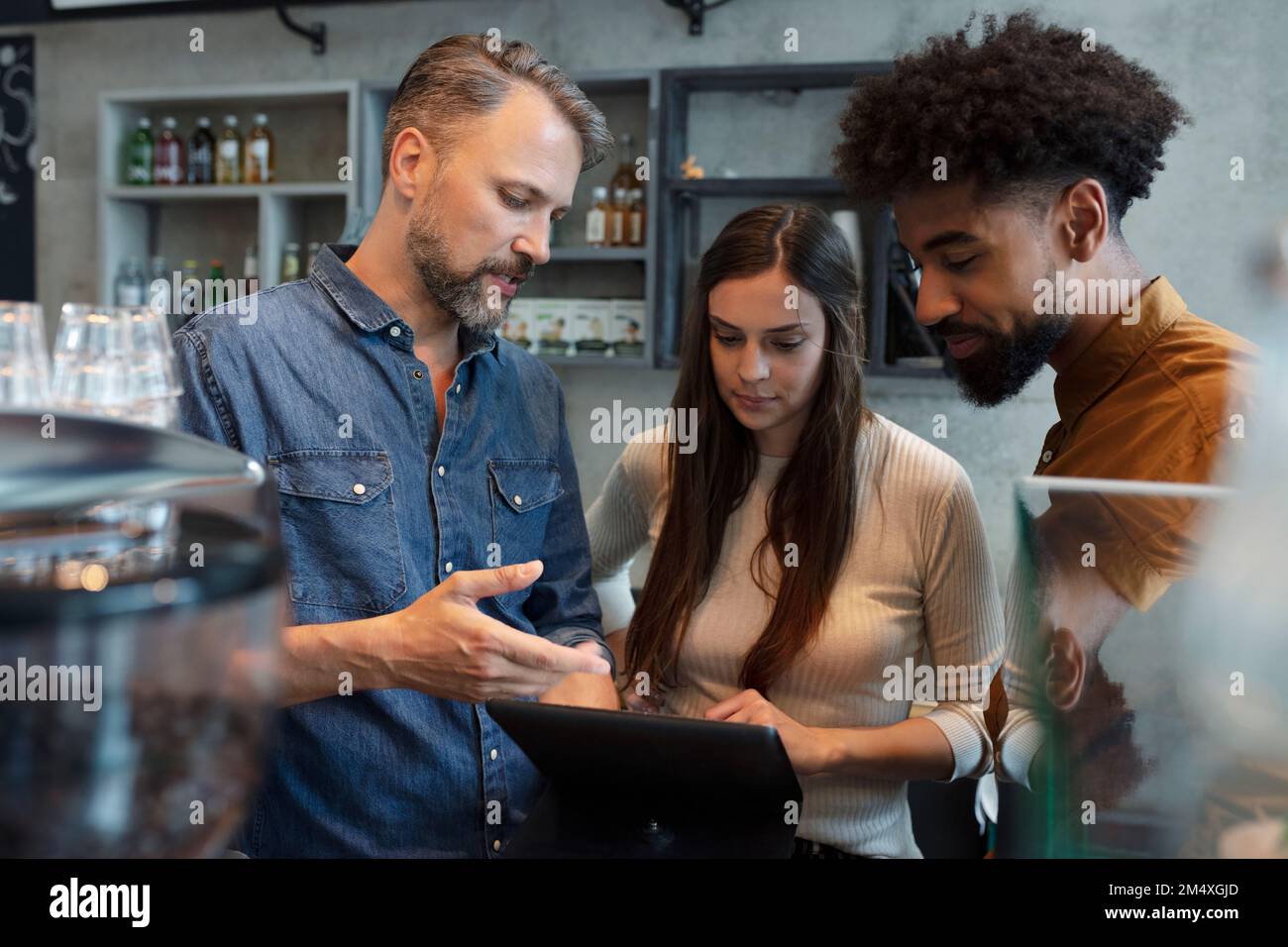 Cafe owner sharing tablet PC with baristas in coffee shop Stock Photo ...