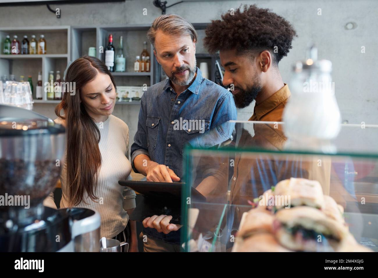 Coffee shop owner sharing tablet PC with baristas in cafe Stock Photo ...