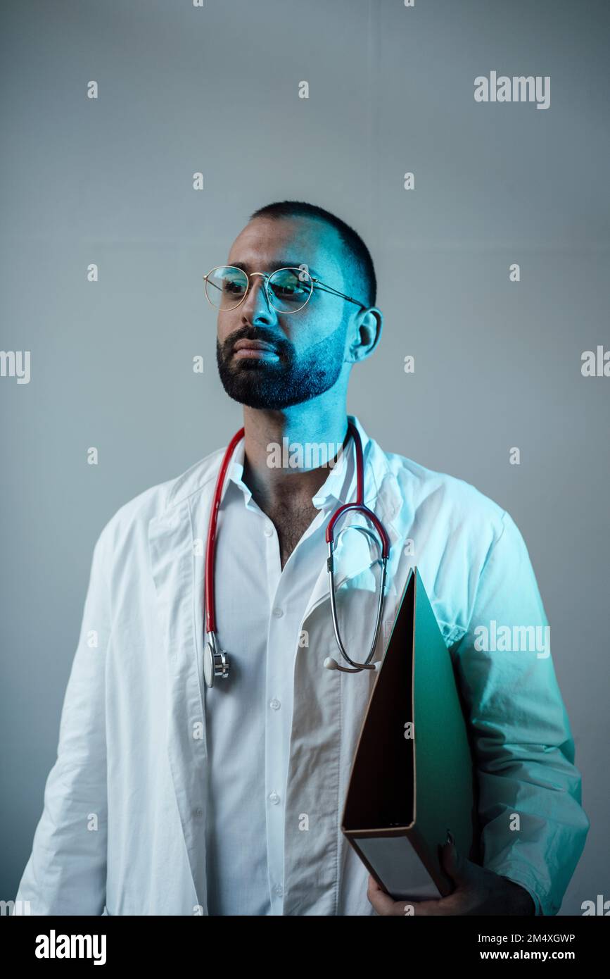 Doctor holding file folder in front of white wall Stock Photo - Alamy