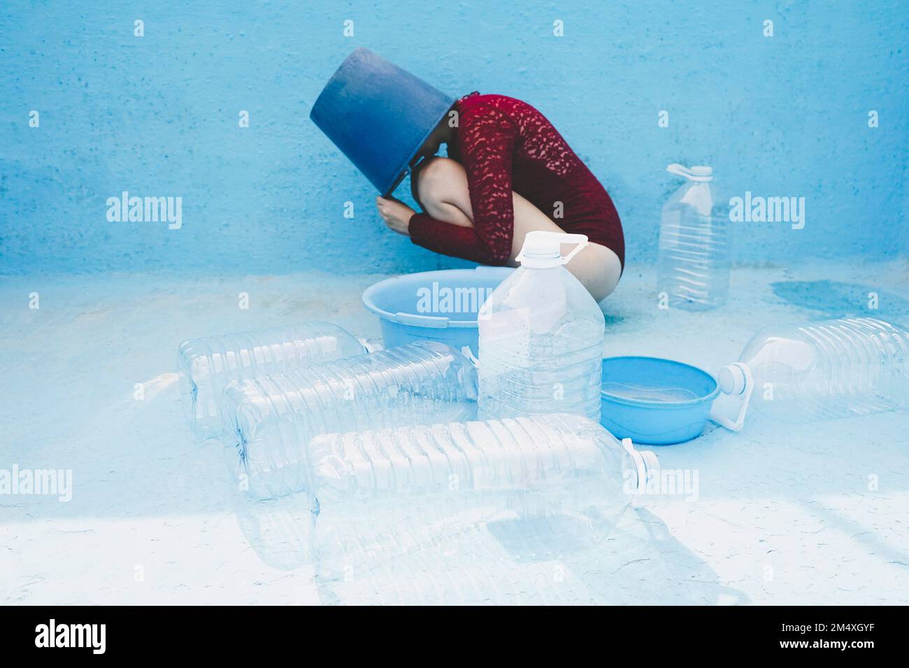 Woman with head inside bucket by plastic bottles in empty swimming pool ...