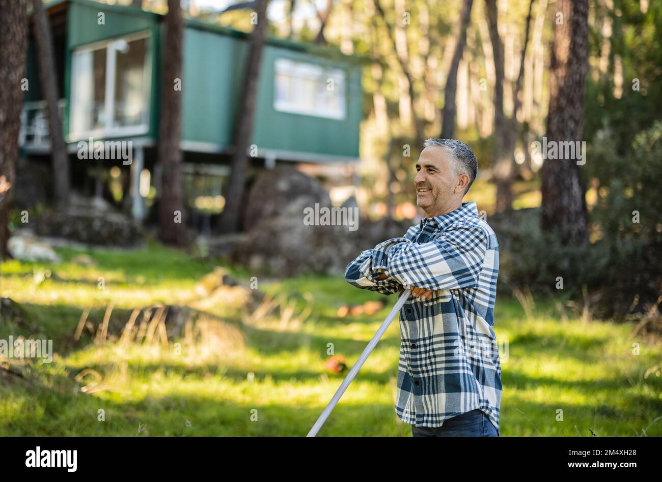 Mature man leaning on rake in natural garden Stock Photo - Alamy