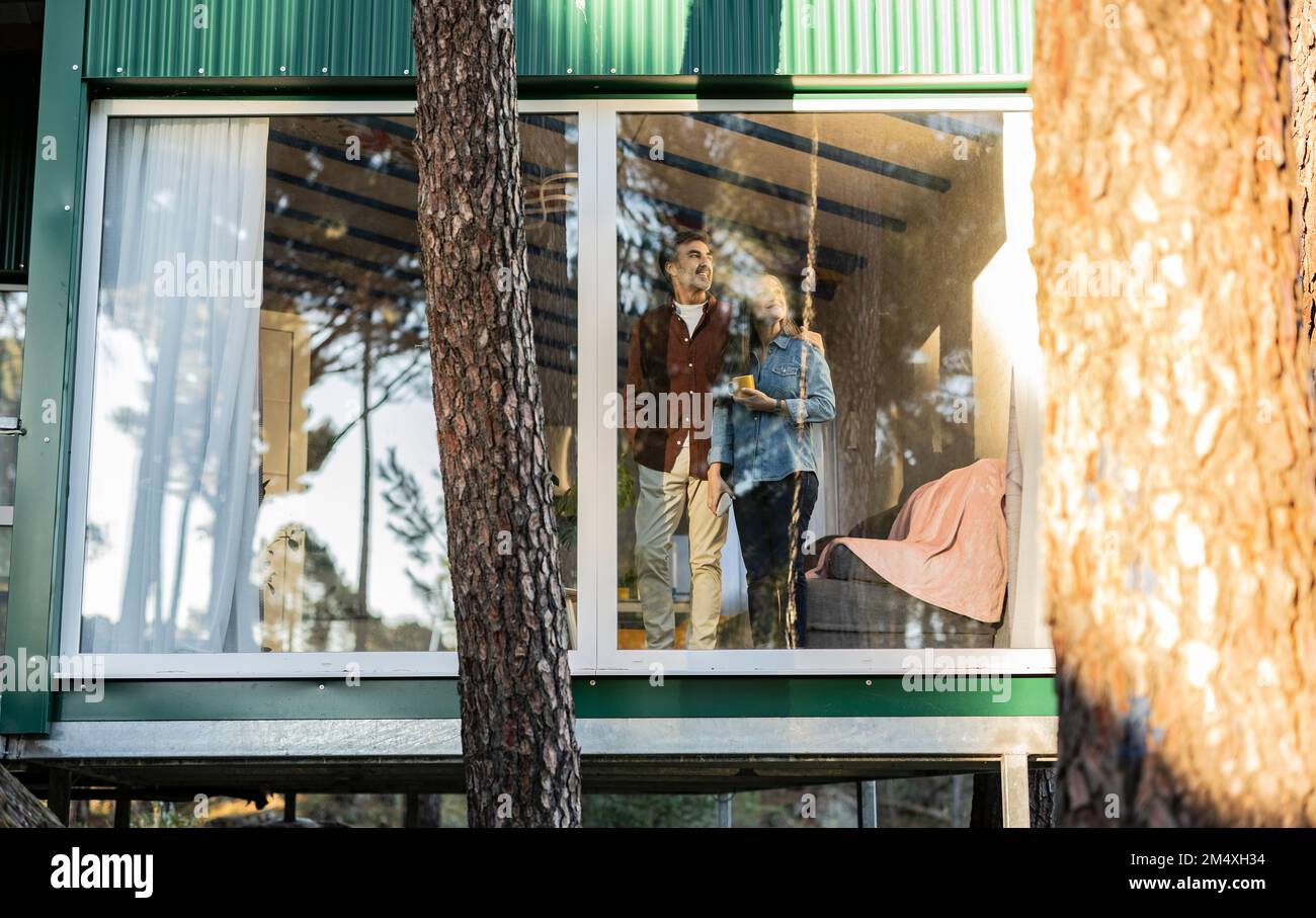 Mature couple standing at the window of a house looking out Stock Photo ...
