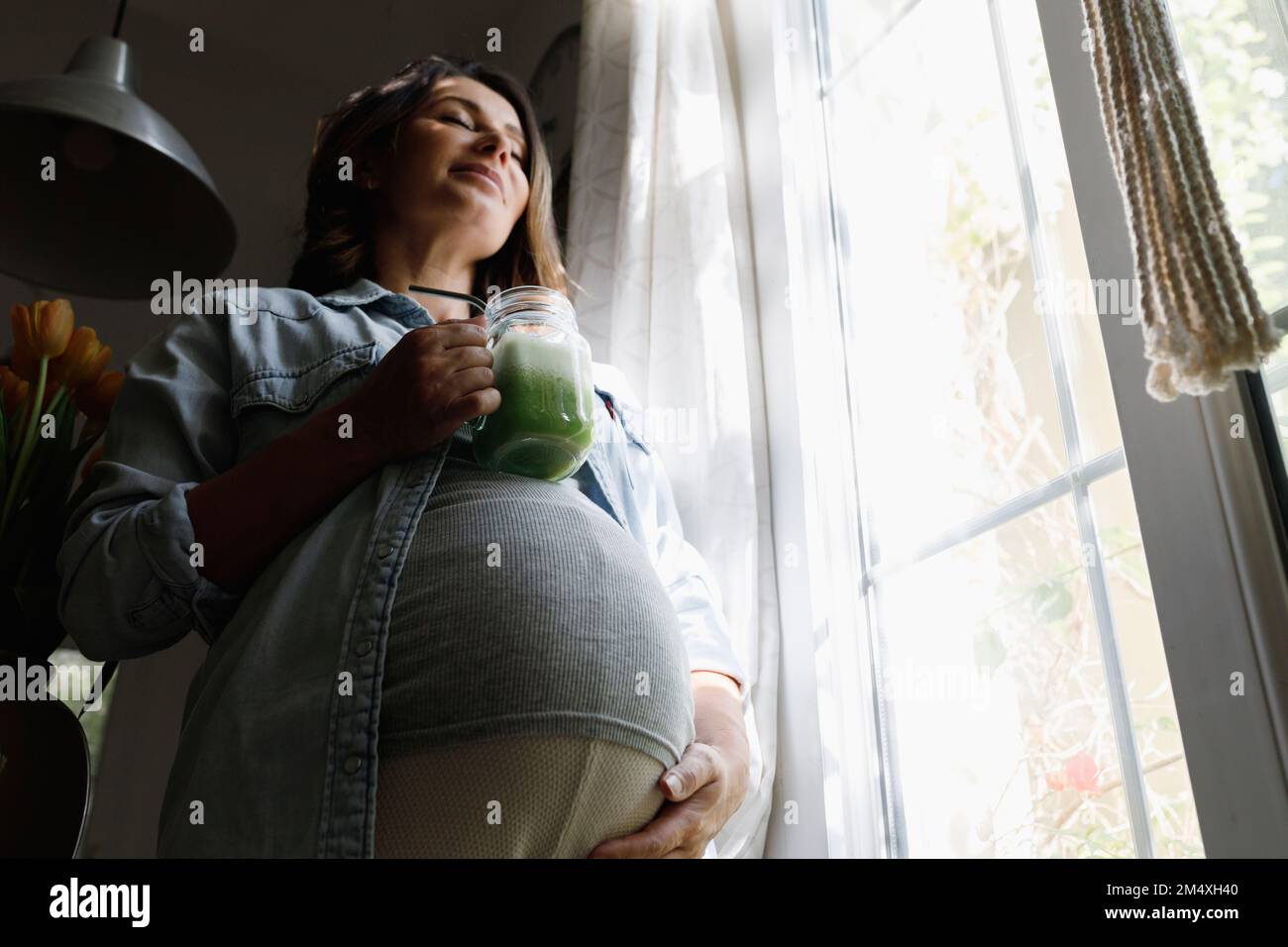 Pregnant woman with glass of green smoothie standing at home Stock ...