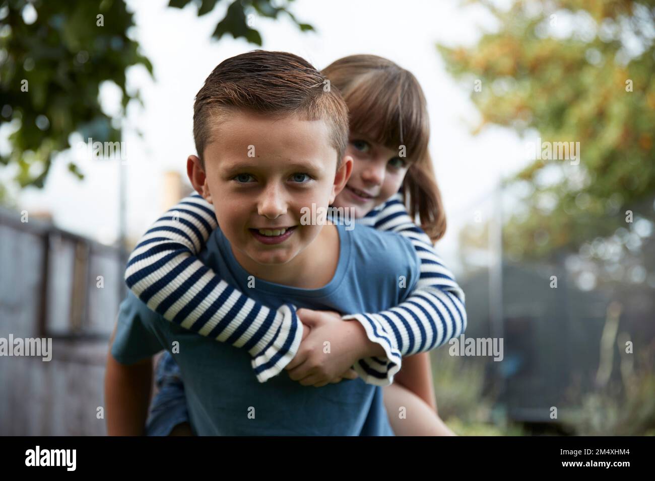 Playful boy giving piggyback ride to sister in garden Stock Photo - Alamy