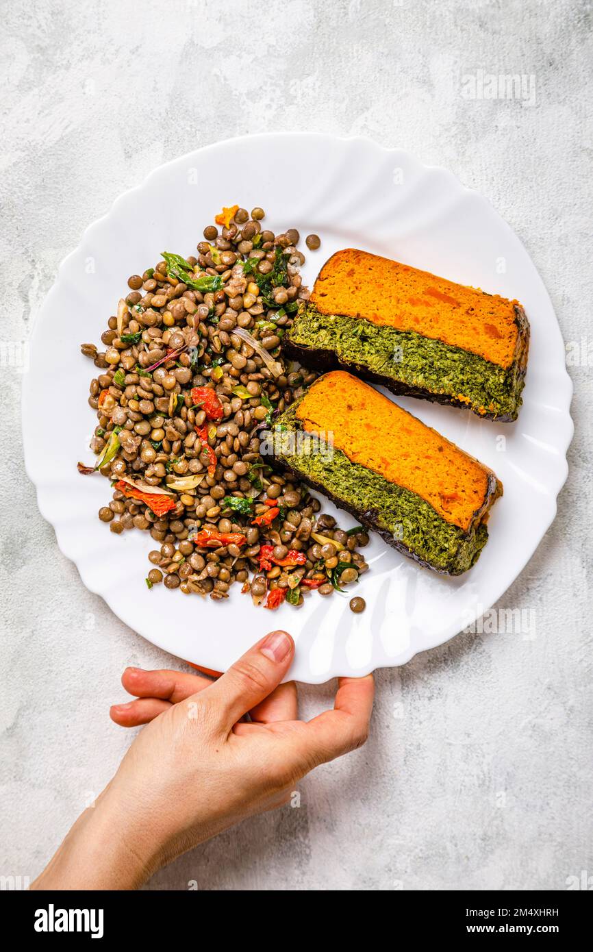 Hand of woman picking up plate of carrot and spinach terrine with ...