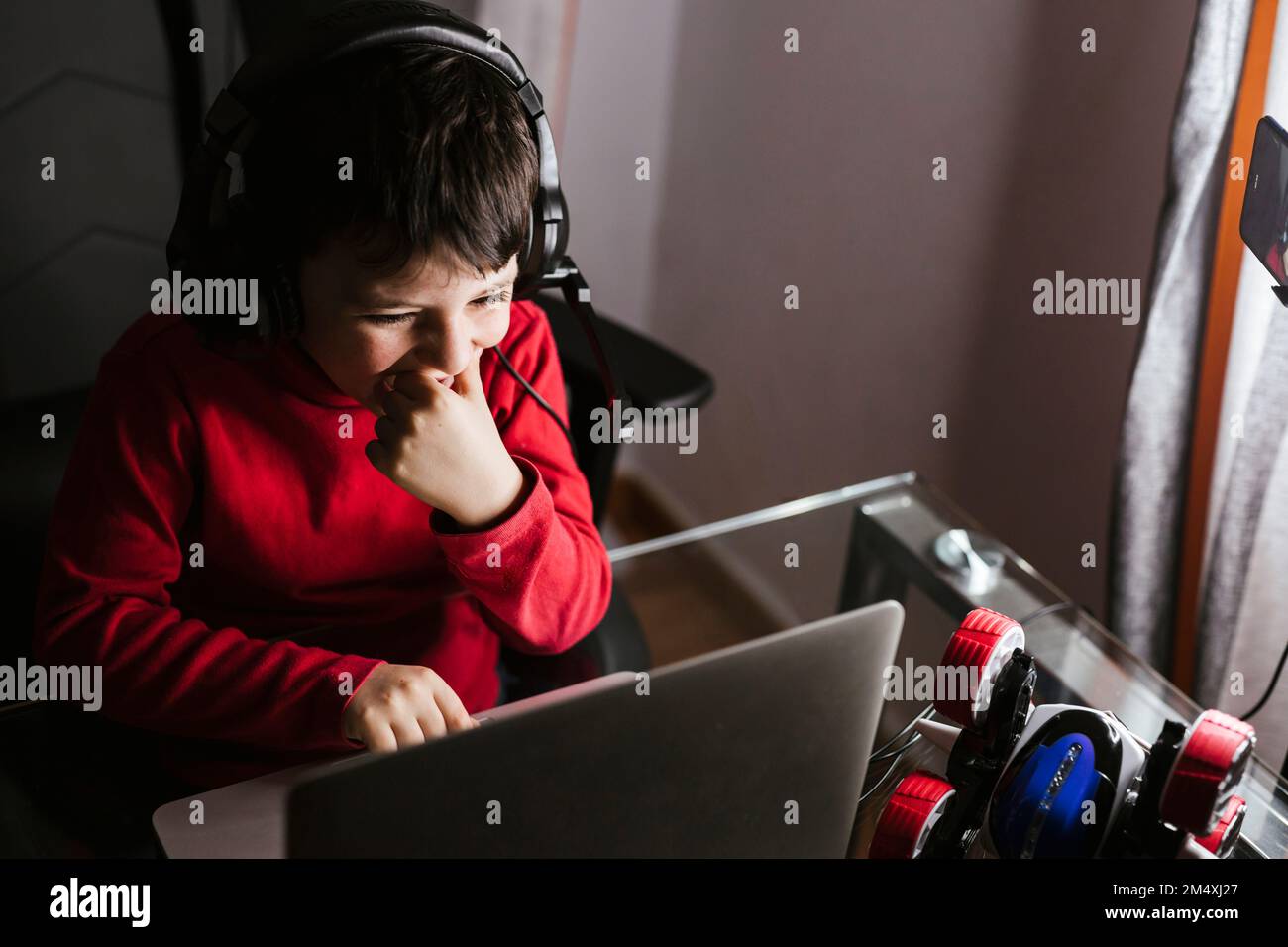 Happy boy wearing headphones using laptop on table Stock Photo - Alamy