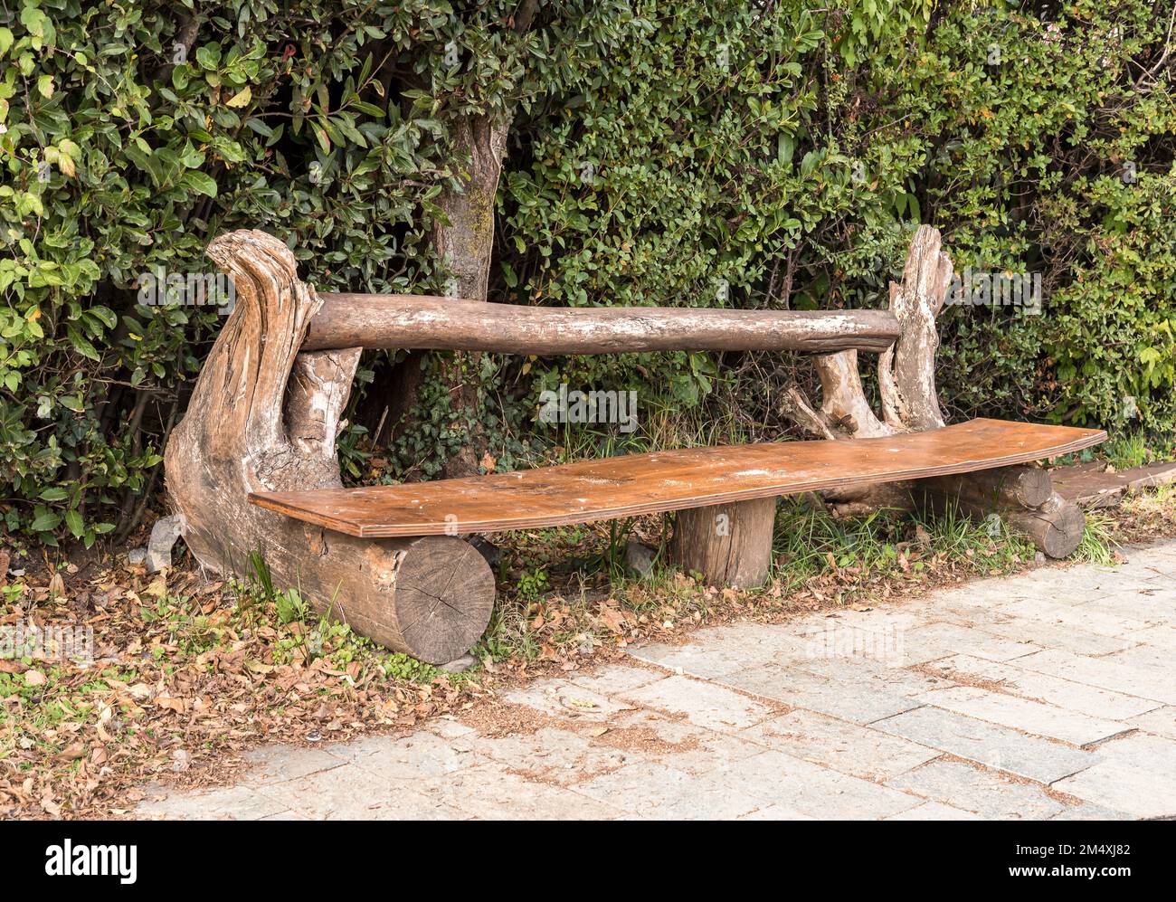Handcrafted wooden bench stands in the park, surrounded by green bushes ...