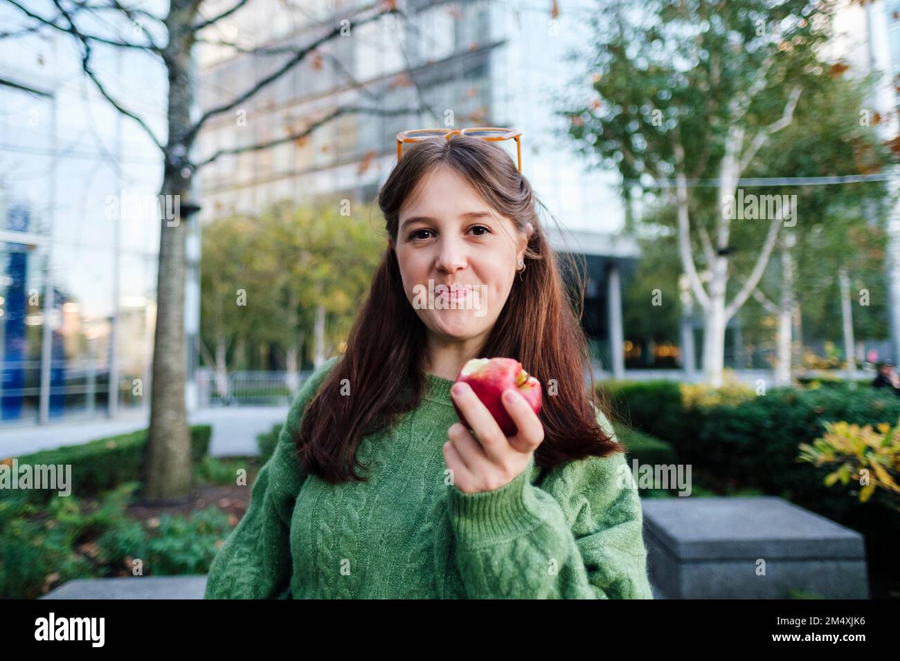 Smiling woman holding apple in front of building Stock Photo - Alamy