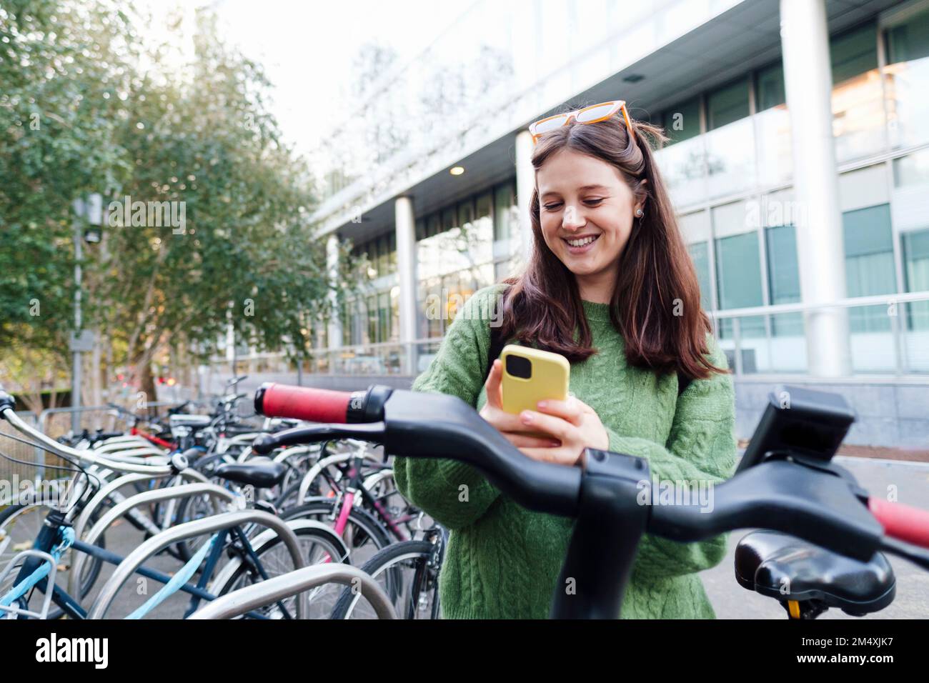 Happy woman renting electric bicycle through smart phone at station ...