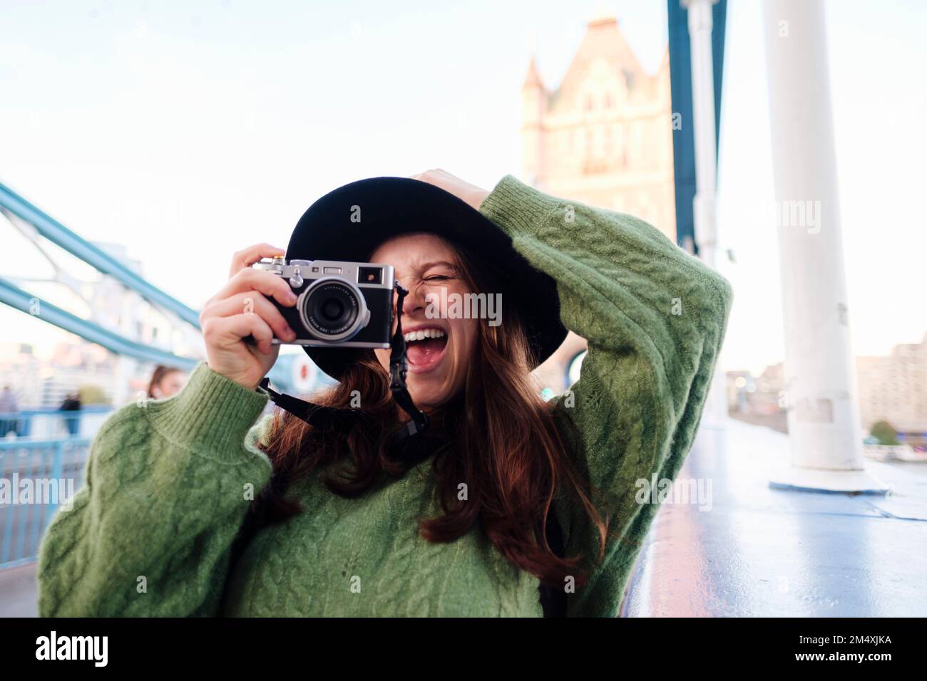 Happy young woman photographing through camera on Tower Bridge, London ...