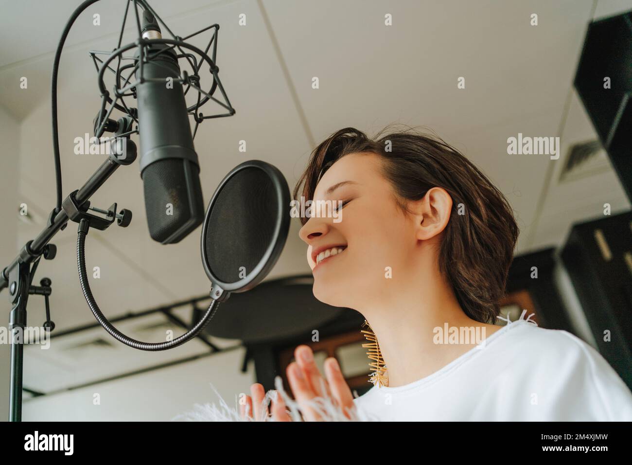 Smiling singer recording music through microphone in studio Stock Photo ...