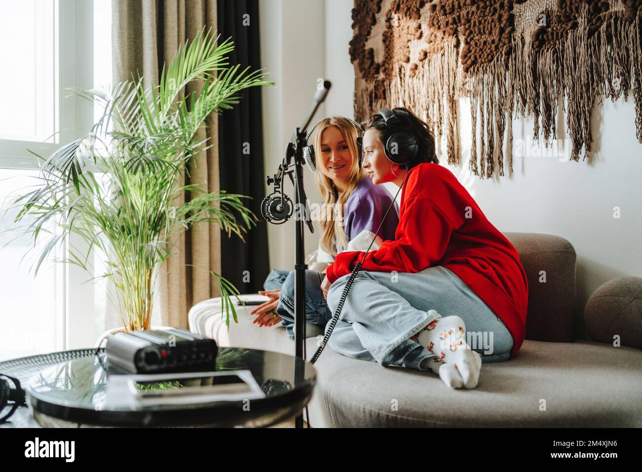 Musician with colleague wearing headphones on sofa in recording studio ...