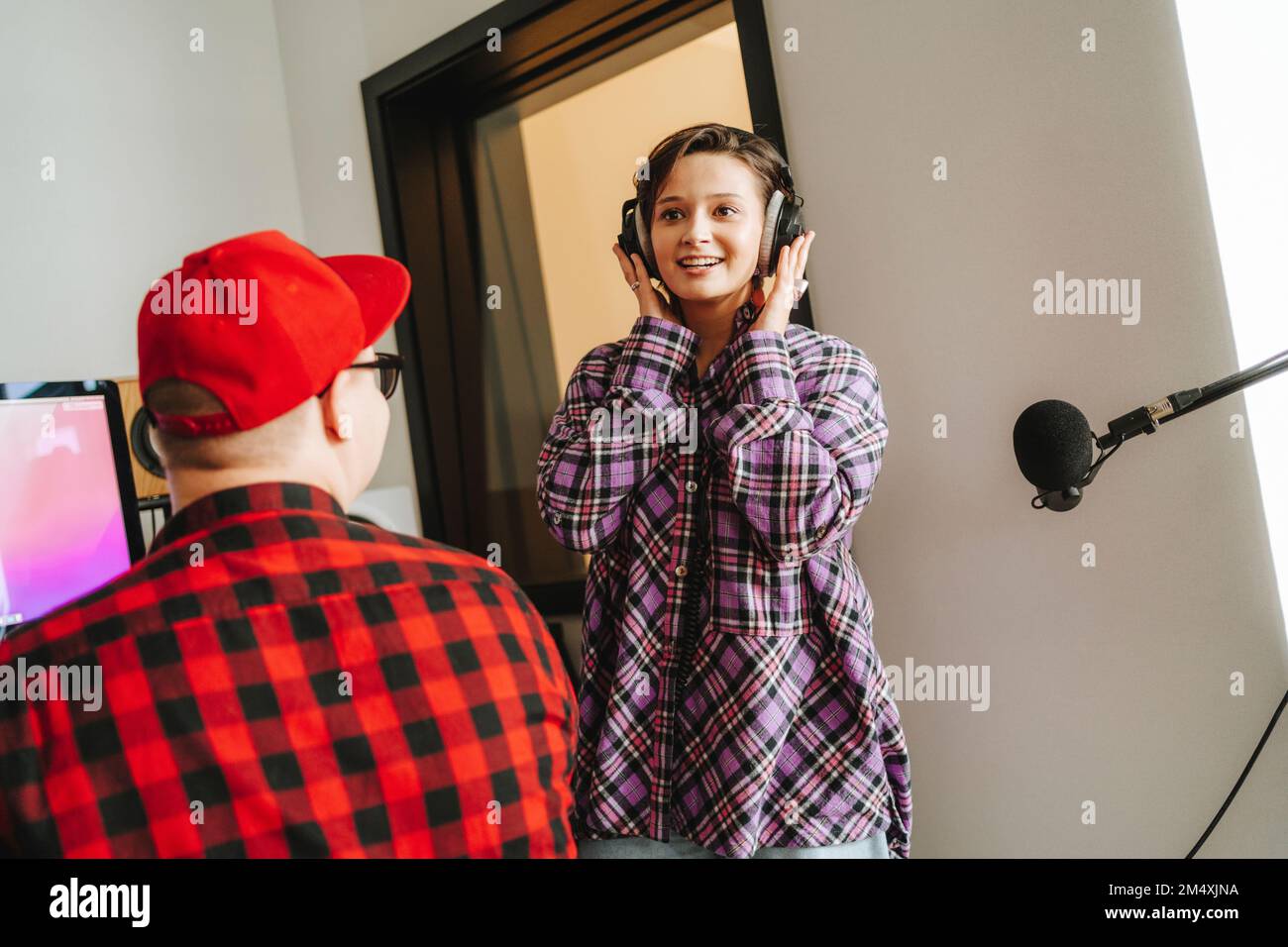 Smiling singer wearing headphones singing in front of colleague at ...