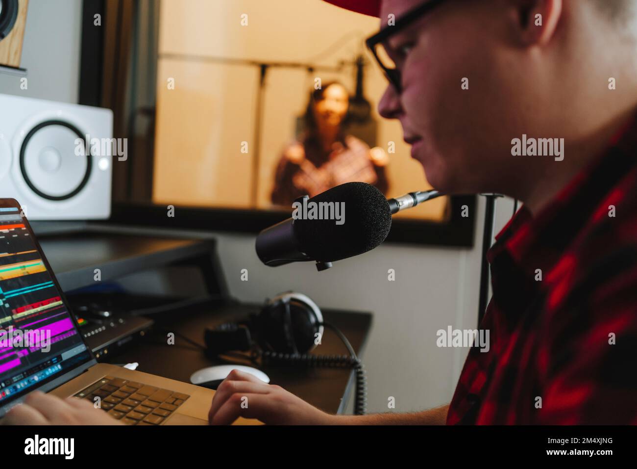 Sound engineer composing on laptop with singer in background at ...